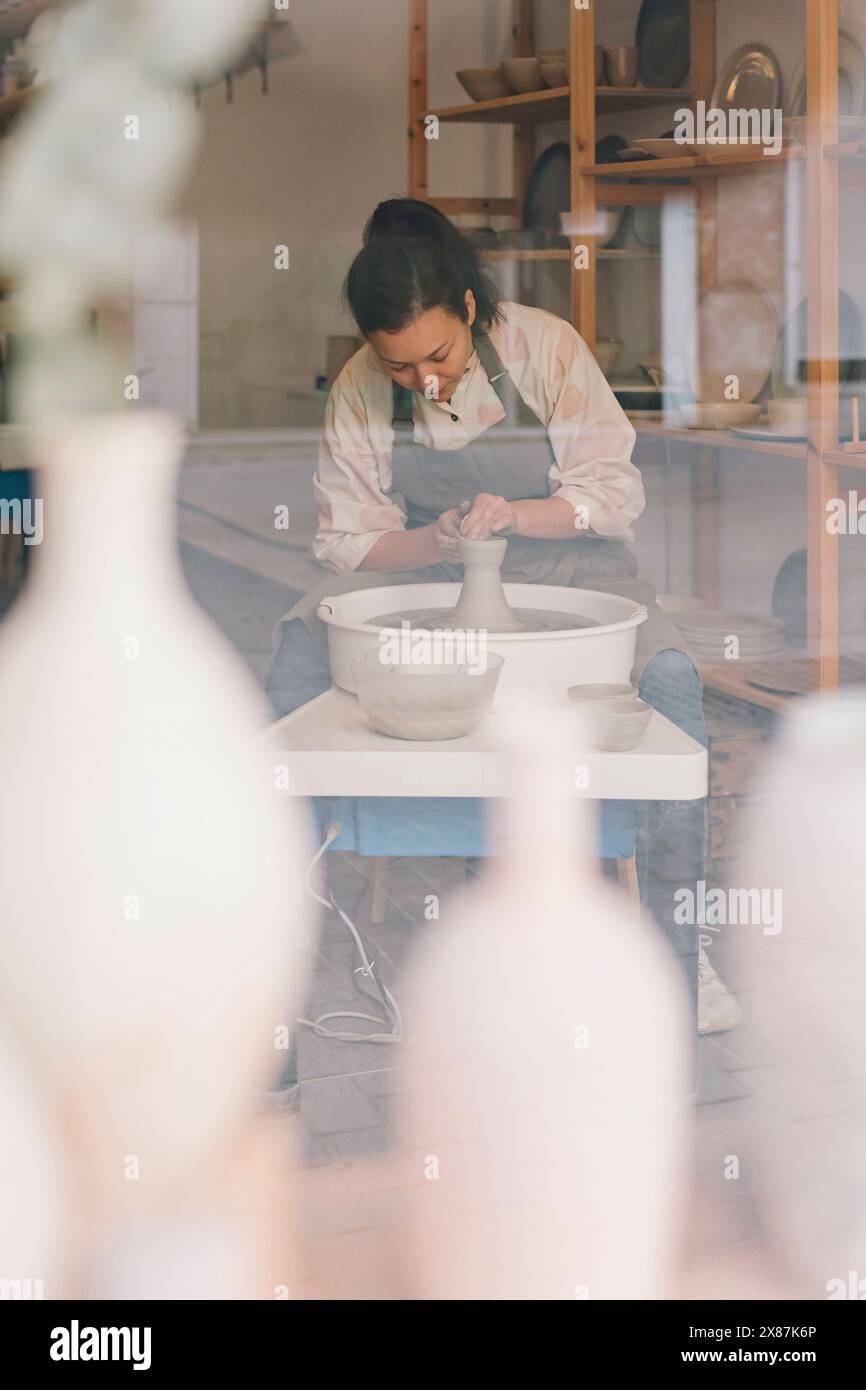 Artist molding clay on pottery wheel seen through window Stock Photo ...