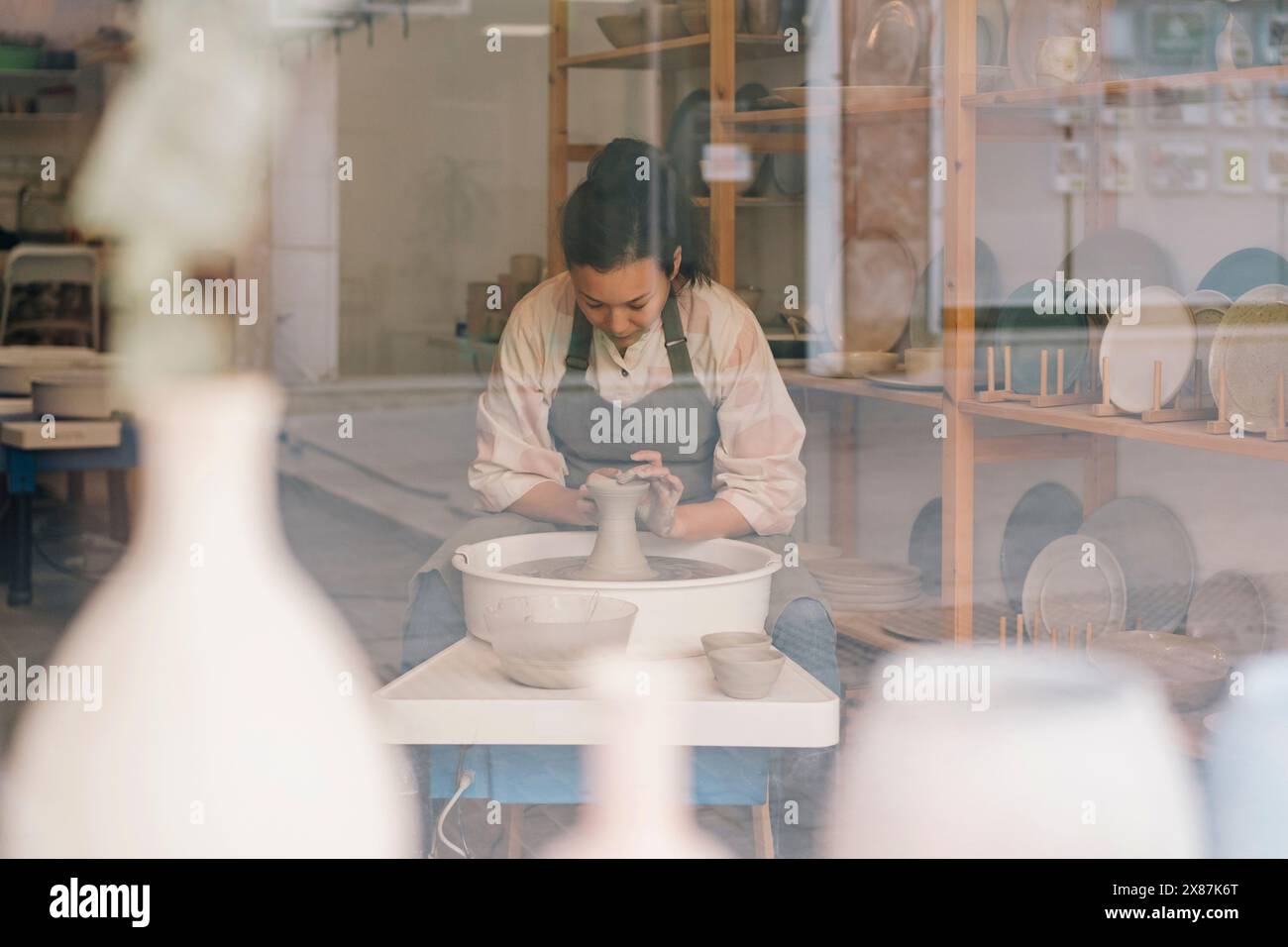 Craftsperson molding clay on pottery wheel seen through window Stock ...