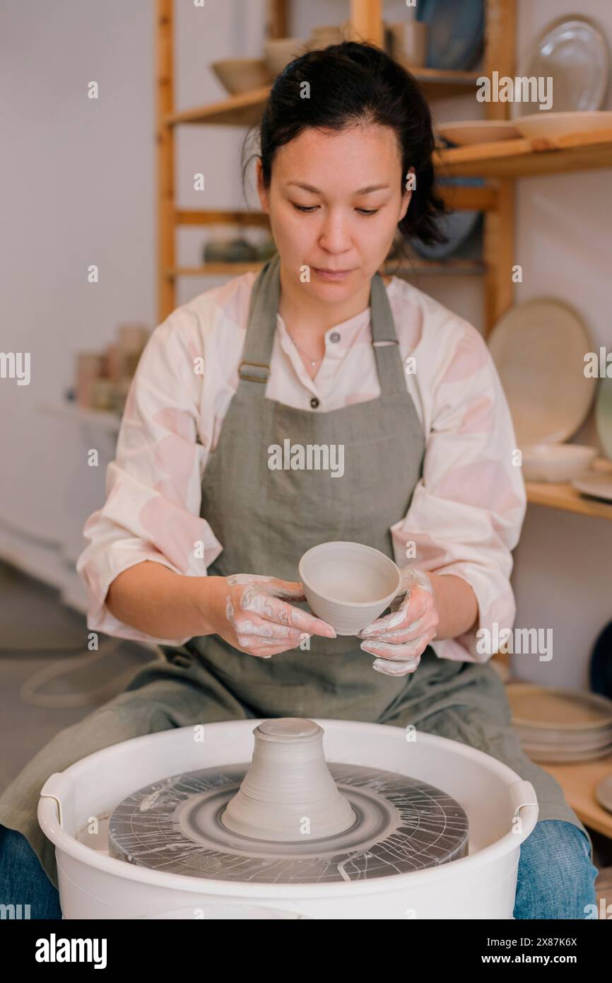 Confident craftsperson with clay bowl over pottery wheel at art studio ...