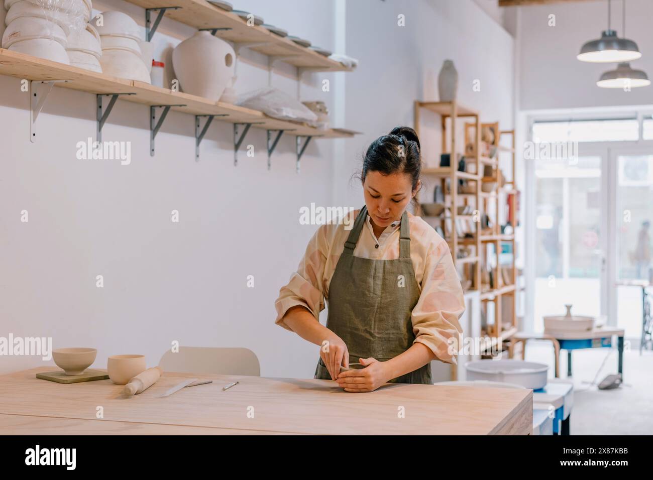 Skilled craftsperson molding clay standing by table at pottery ...