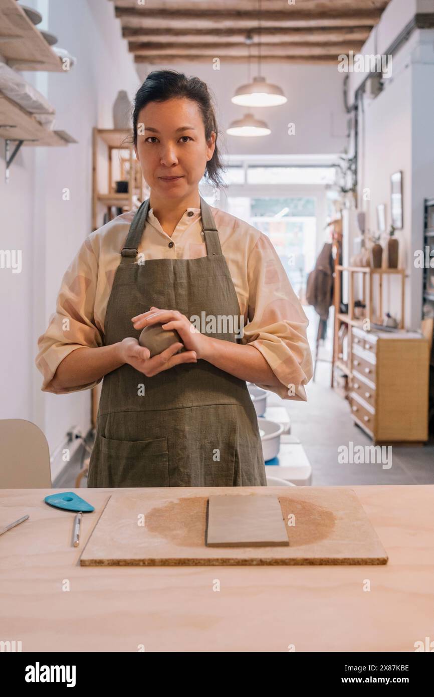 Skilled craftsperson molding clay standing by table at pottery ...