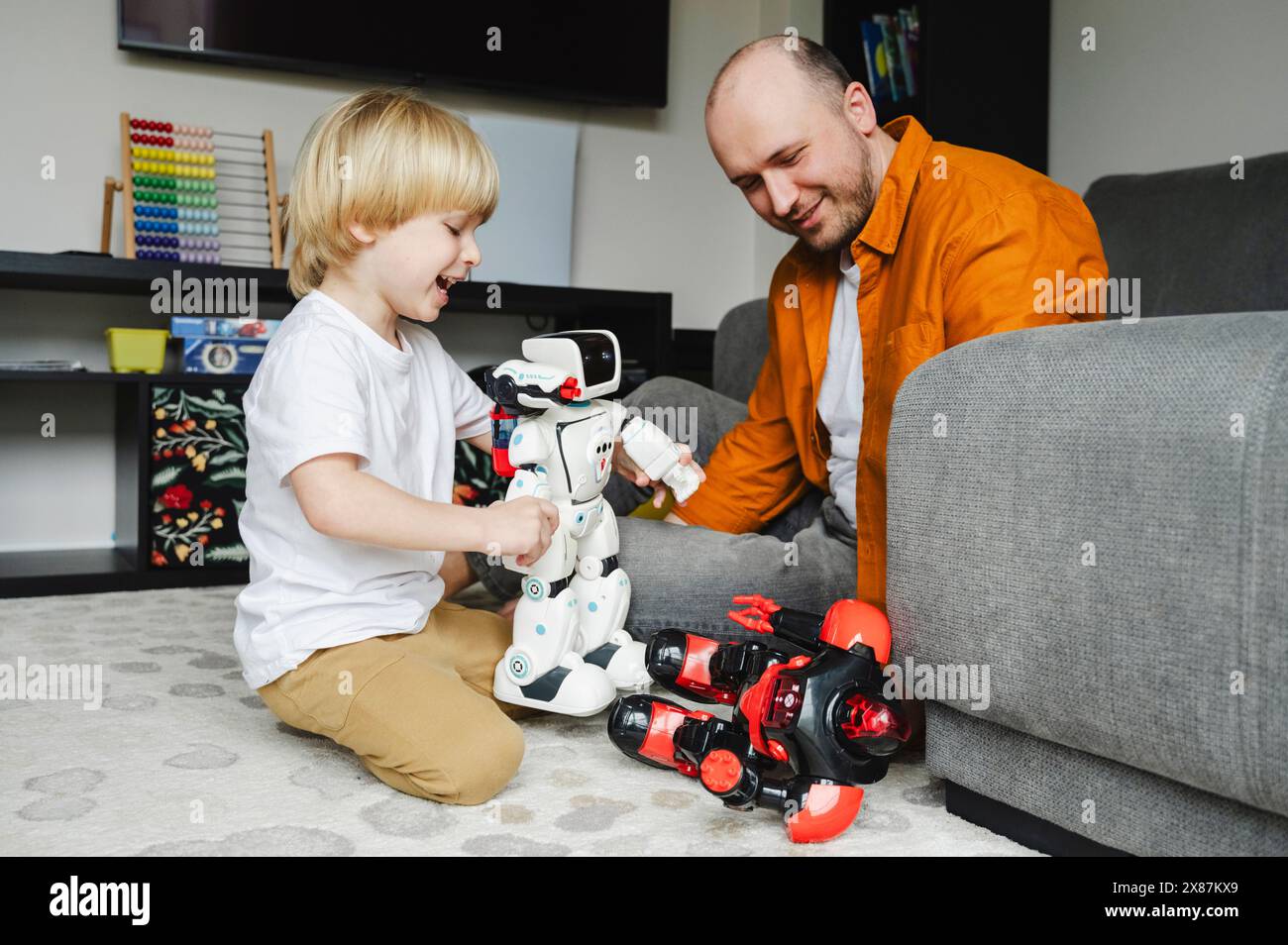 Smiling son playing with robots sitting next to father at home Stock ...