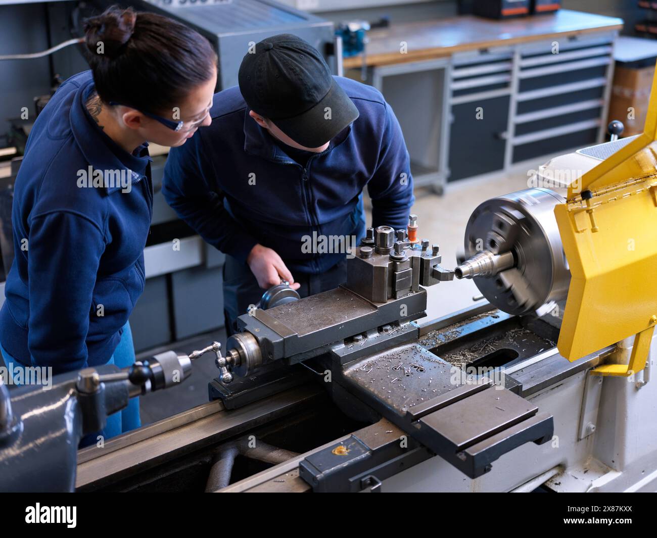Engineer teaching trainee to operate lathe machine at metal industry ...