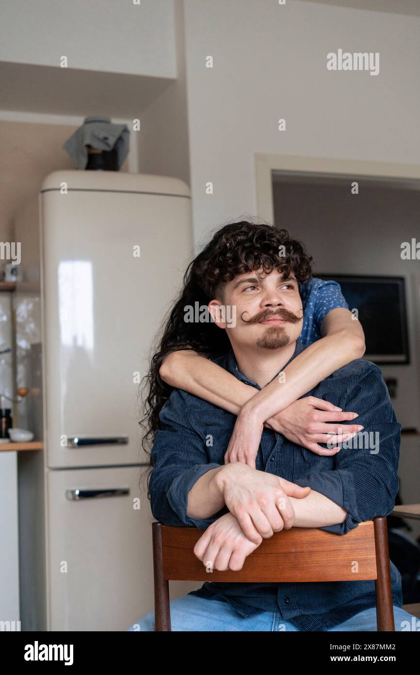 Woman hiding behind boyfriend sitting on chair at home Stock Photo - Alamy