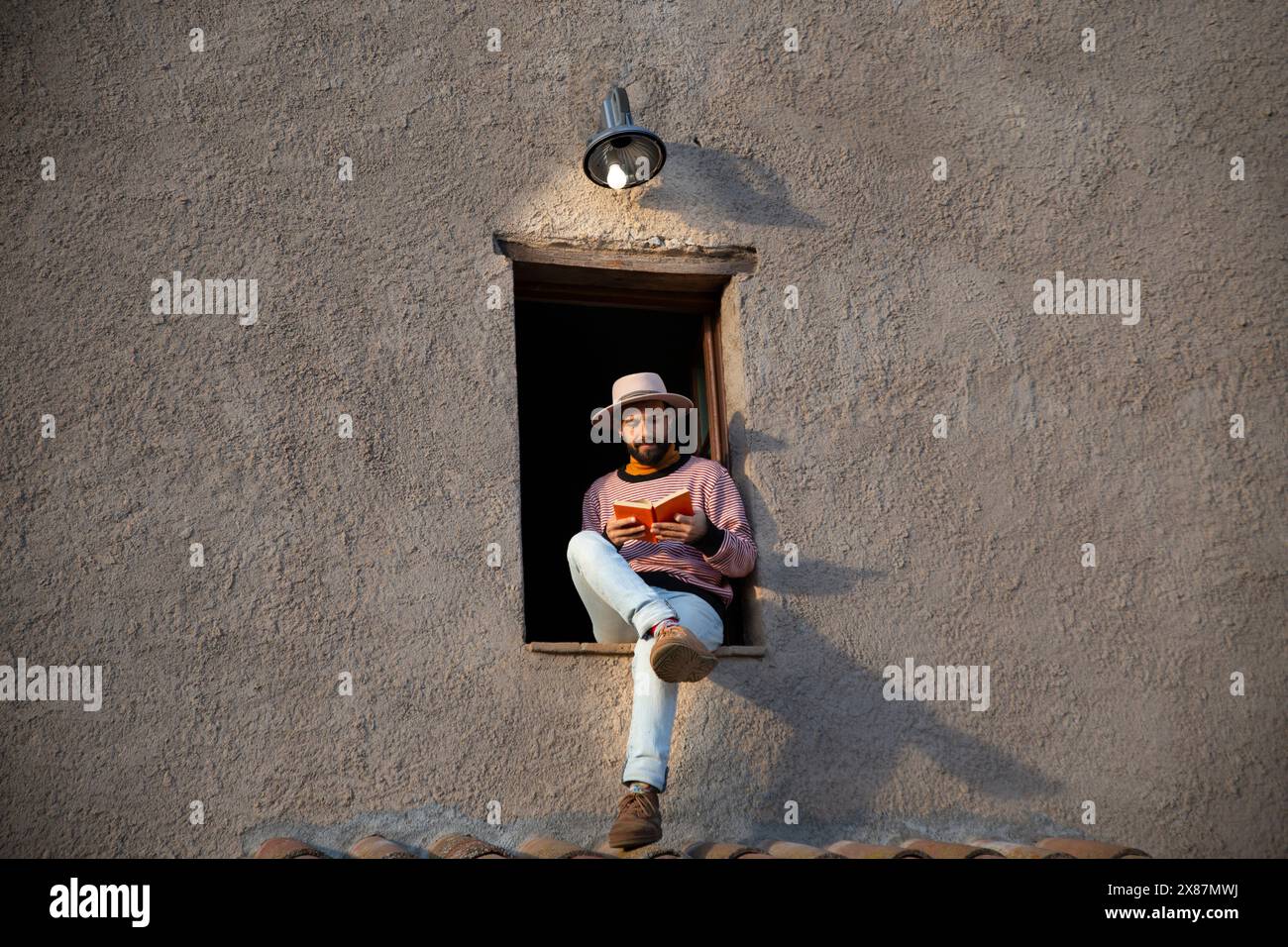 Man sitting on window and reading book Stock Photo - Alamy