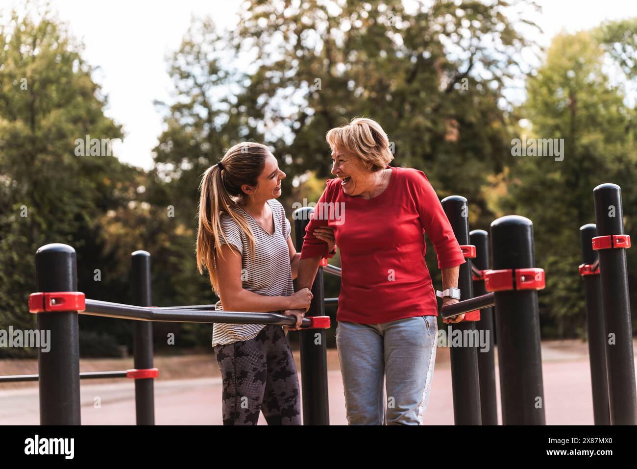 Happy woman guiding grandmother practicing exercise on gymnastics bars ...