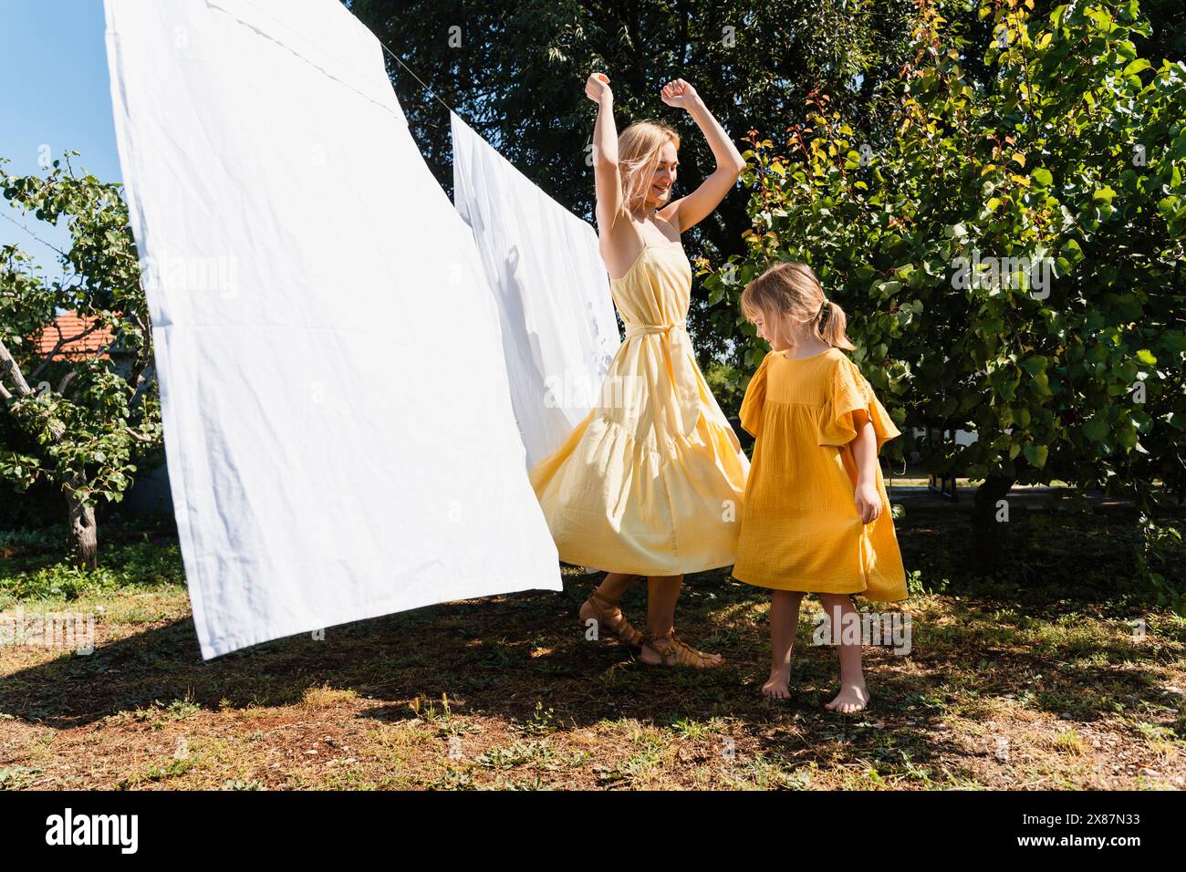 Mother and daughter dancing by white bedsheet hanging on clothesline at ...