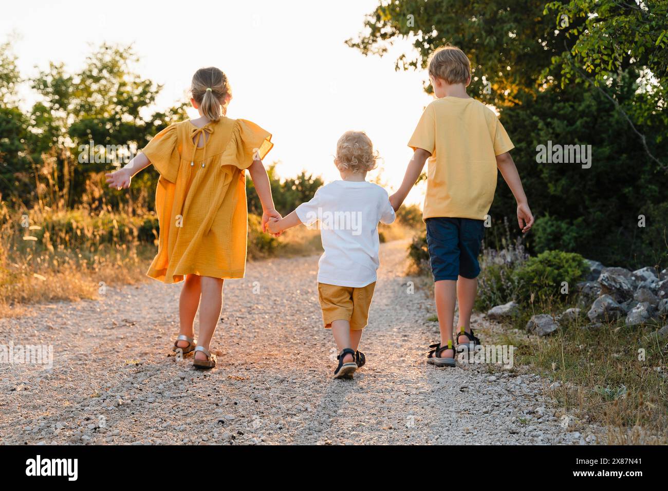 Siblings holding hands walking together on footpath at sunset Stock ...