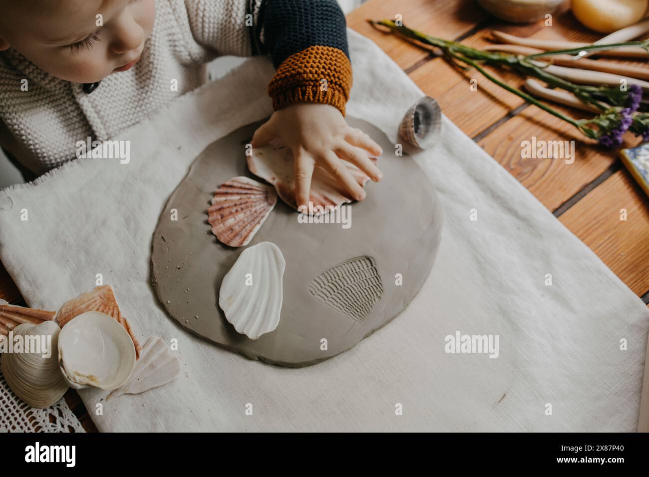 Boy making imprint of shells on clay at home Stock Photo - Alamy