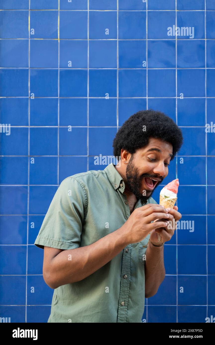 Happy Young Man Holding Ice Cream Cone In Front Of Blue Tile Wall Stock