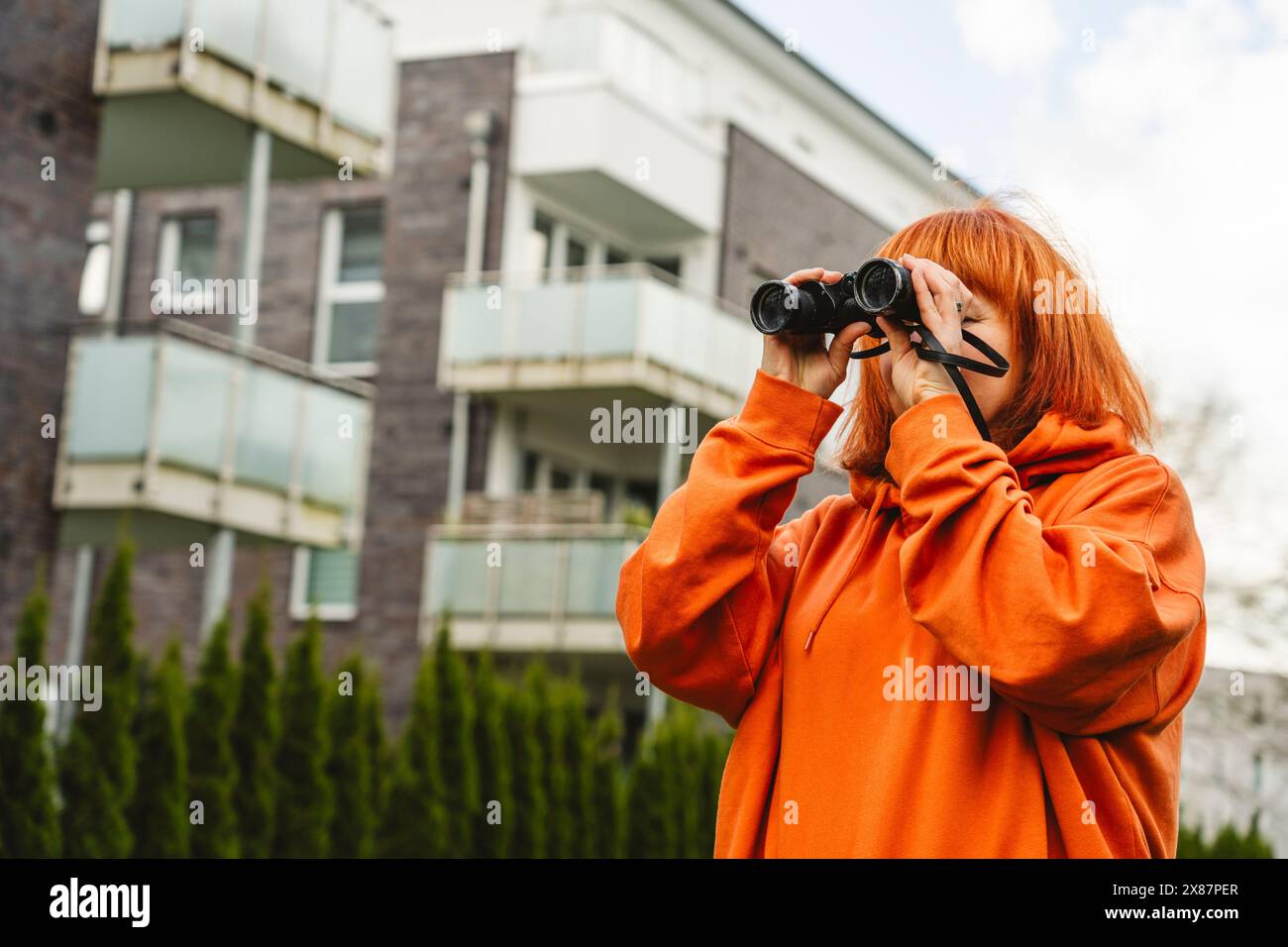 Redhead woman watching through binoculars in front of building Stock Photo - Alamy
