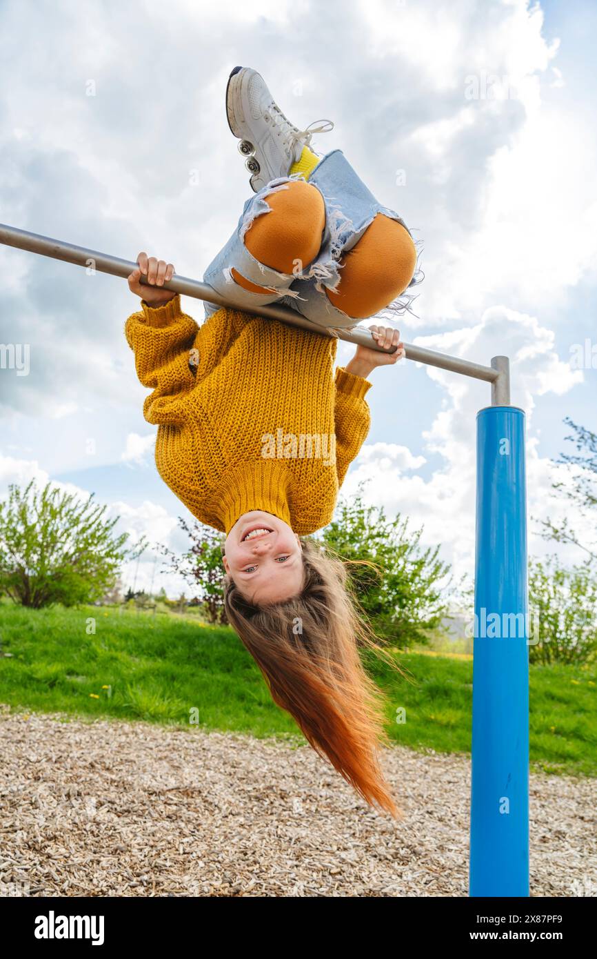 Cheerful girl hanging upside down on gymnastics bar at playground Stock Photo - Alamy