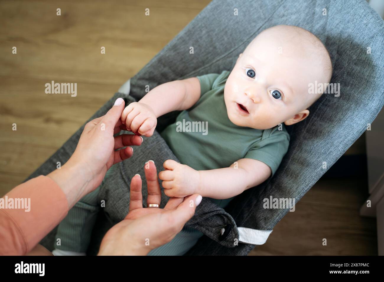 Cute baby boy on rocking chair holding hands of mother in kitchen Stock ...