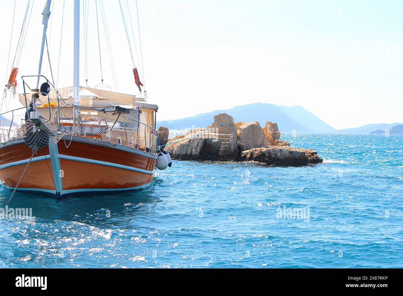 Yacht with folded sail with white and brown sloop is anchored to rock ...