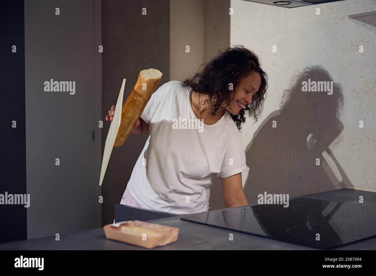 Multi ethnic young adult woman smiling broadly, holding a loaf of bread ...