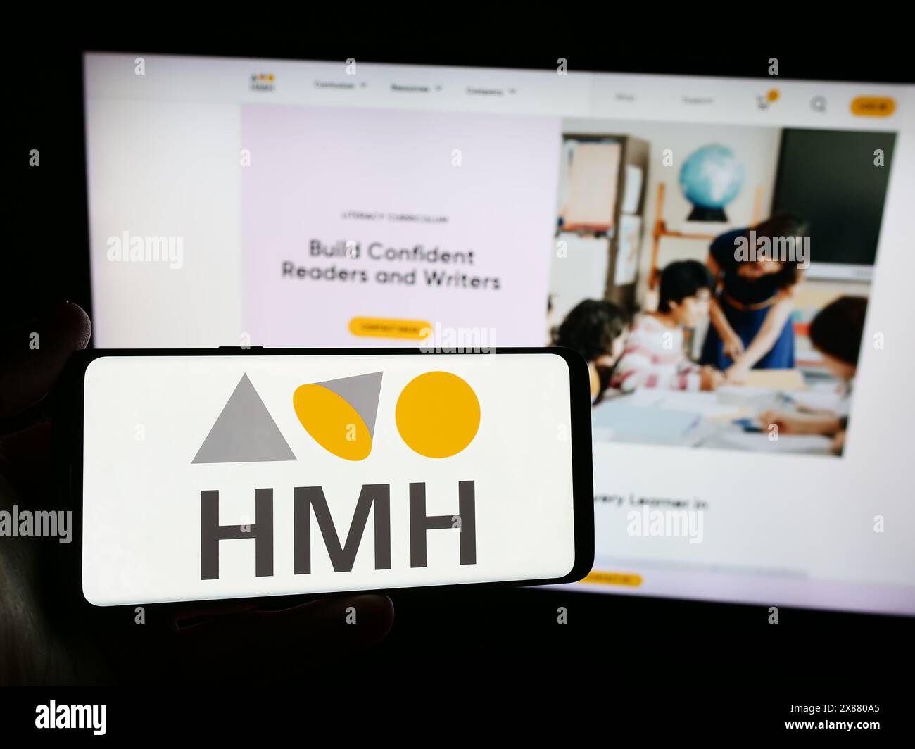 Person holding smartphone with logo of Houghton Mifflin Harcourt Publishing Company (HMH) in ...
