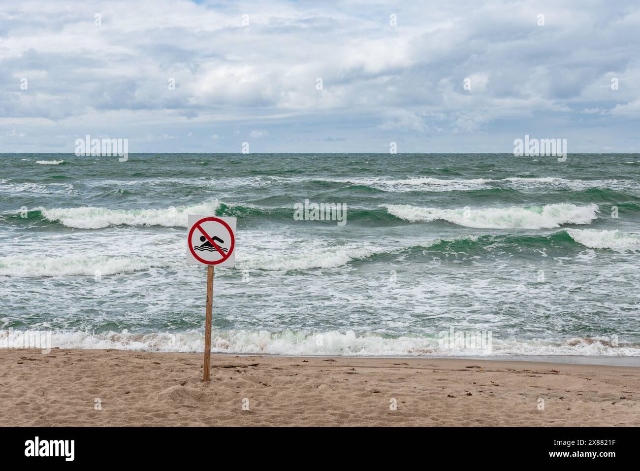 no swimming sign at an empty beach with rough wavy sea in a background ...