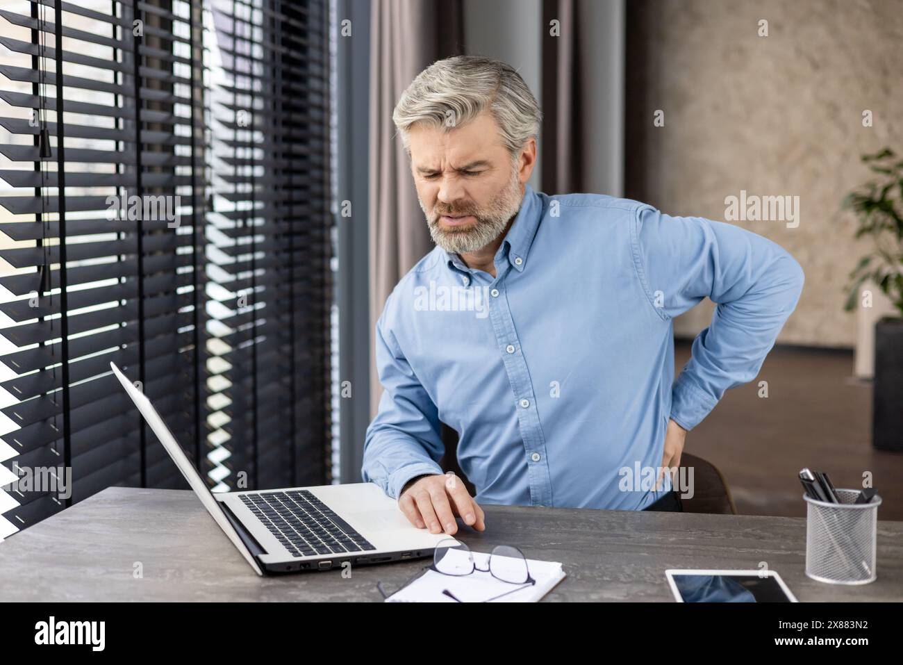 A middleaged man in an office setting experiences discomfort and back ...
