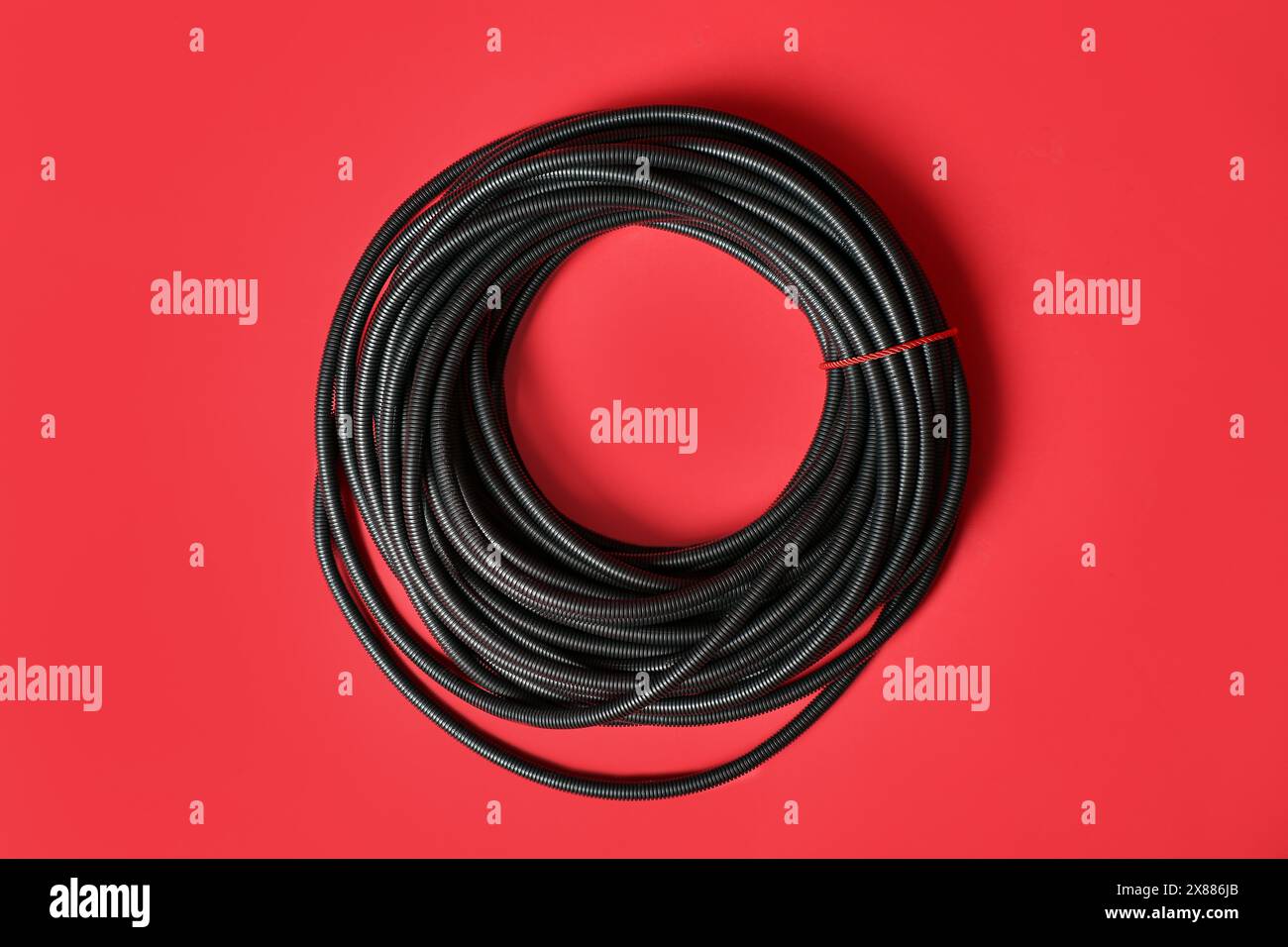 Rolled flexible conduit tube on red background Stock Photo - Alamy