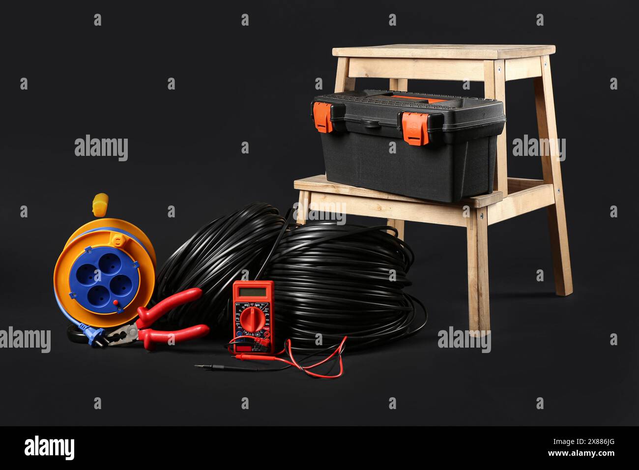 Multimeter, rolled wires, toolbox and extension cable reel on black ...