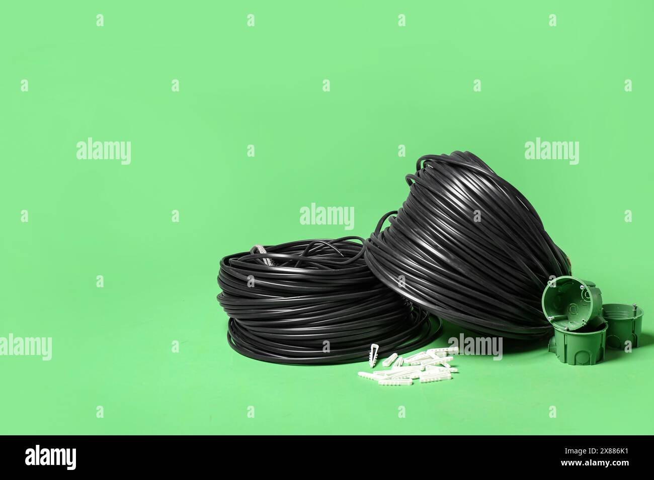 Rolled cables, wall plugs and socket mounting boxes on green background ...