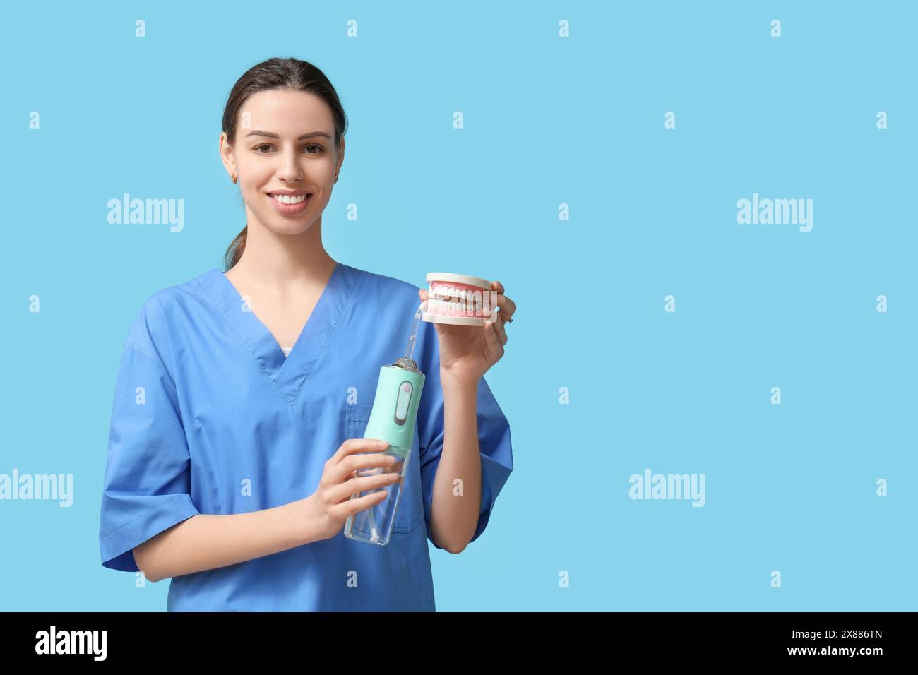 Female dentist with oral irrigator and jaw model on blue background ...