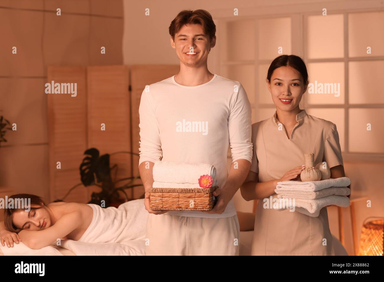 Massage therapists with towels and client in dark spa salon Stock Photo ...