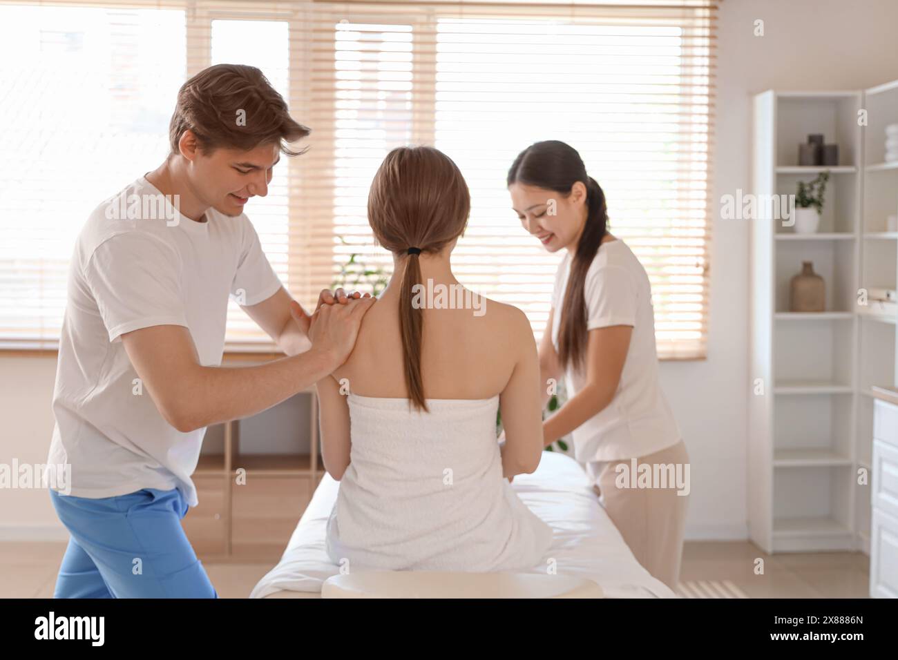 Therapists massaging woman in spa salon, back view Stock Photo - Alamy