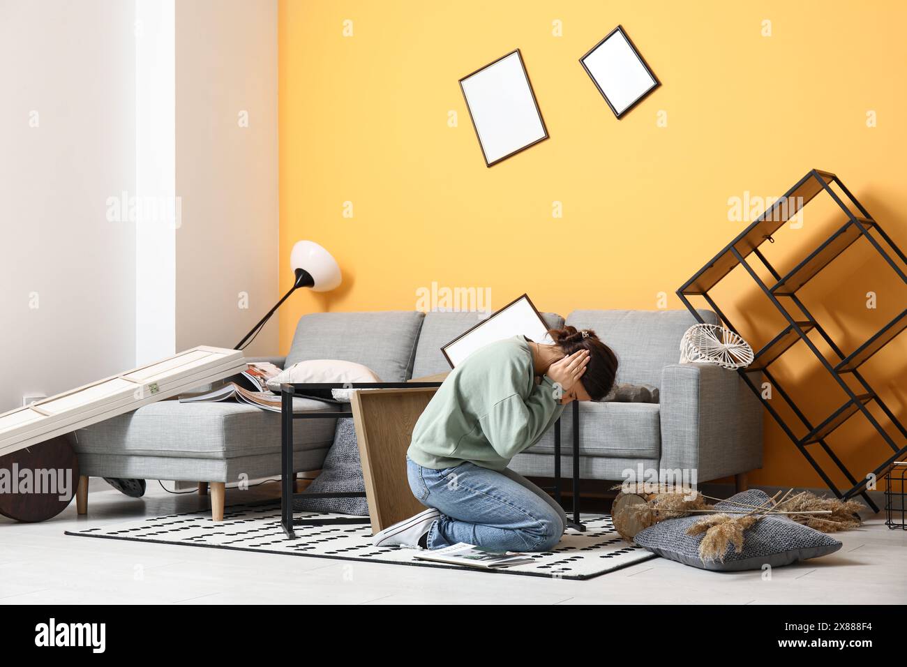 Young woman sitting on floor in living room with messed furniture after ...