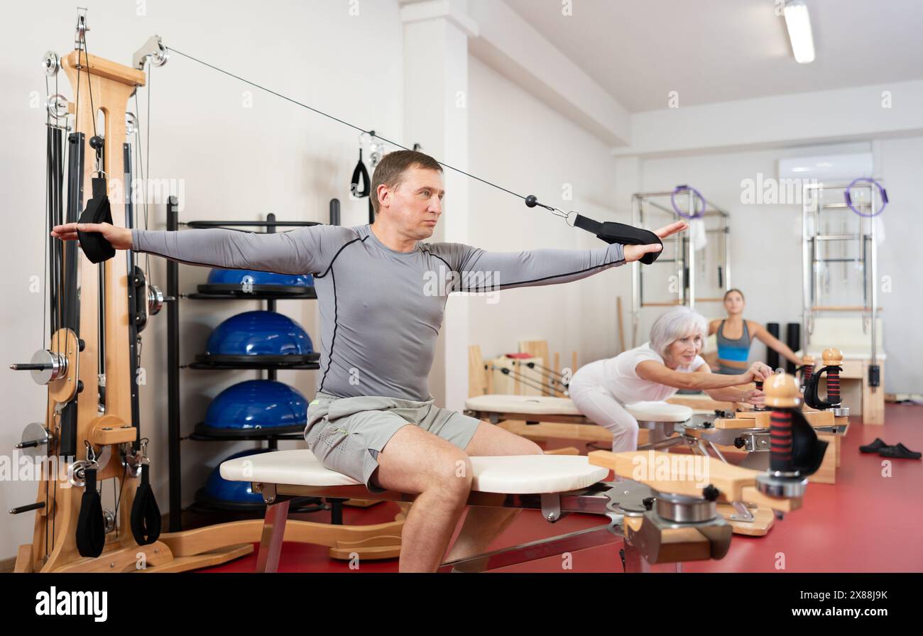 Sports club man client on reformer with cable and rope performs ...