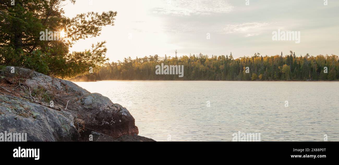 Sunrise behind rocks and pines on a boundary waters lake during autumn ...