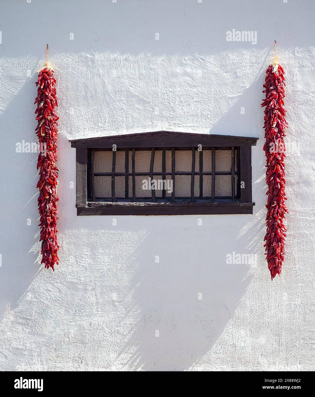 Side lighting of red chili ristras hanging on white wall with black ...