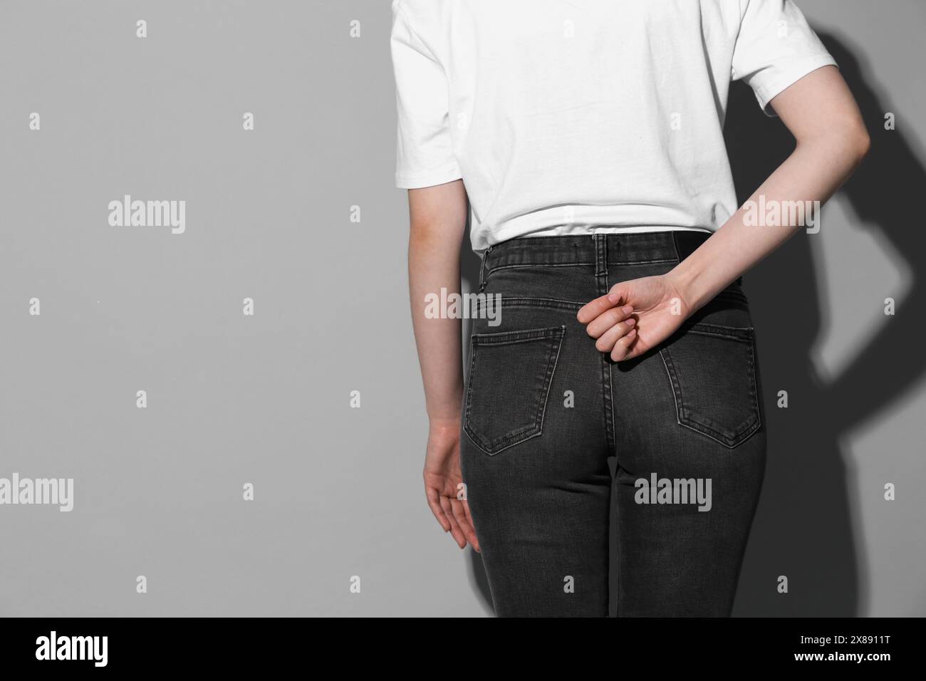 SOS gesture. Woman showing signal for help behind her back on grey ...