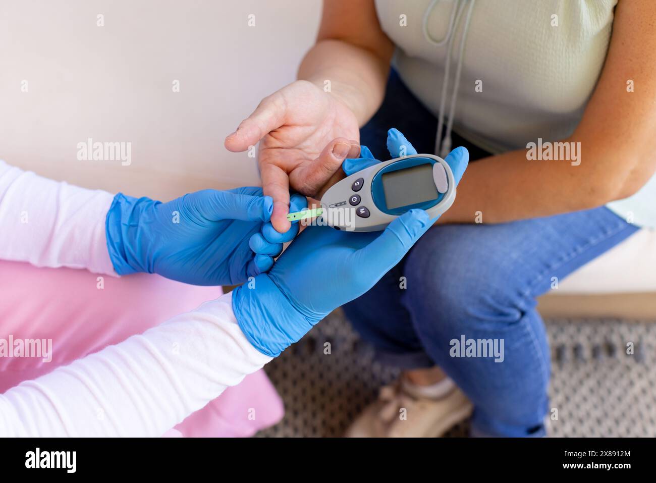 At home, Asian nurse and middle-aged patient check blood sugar levels ...