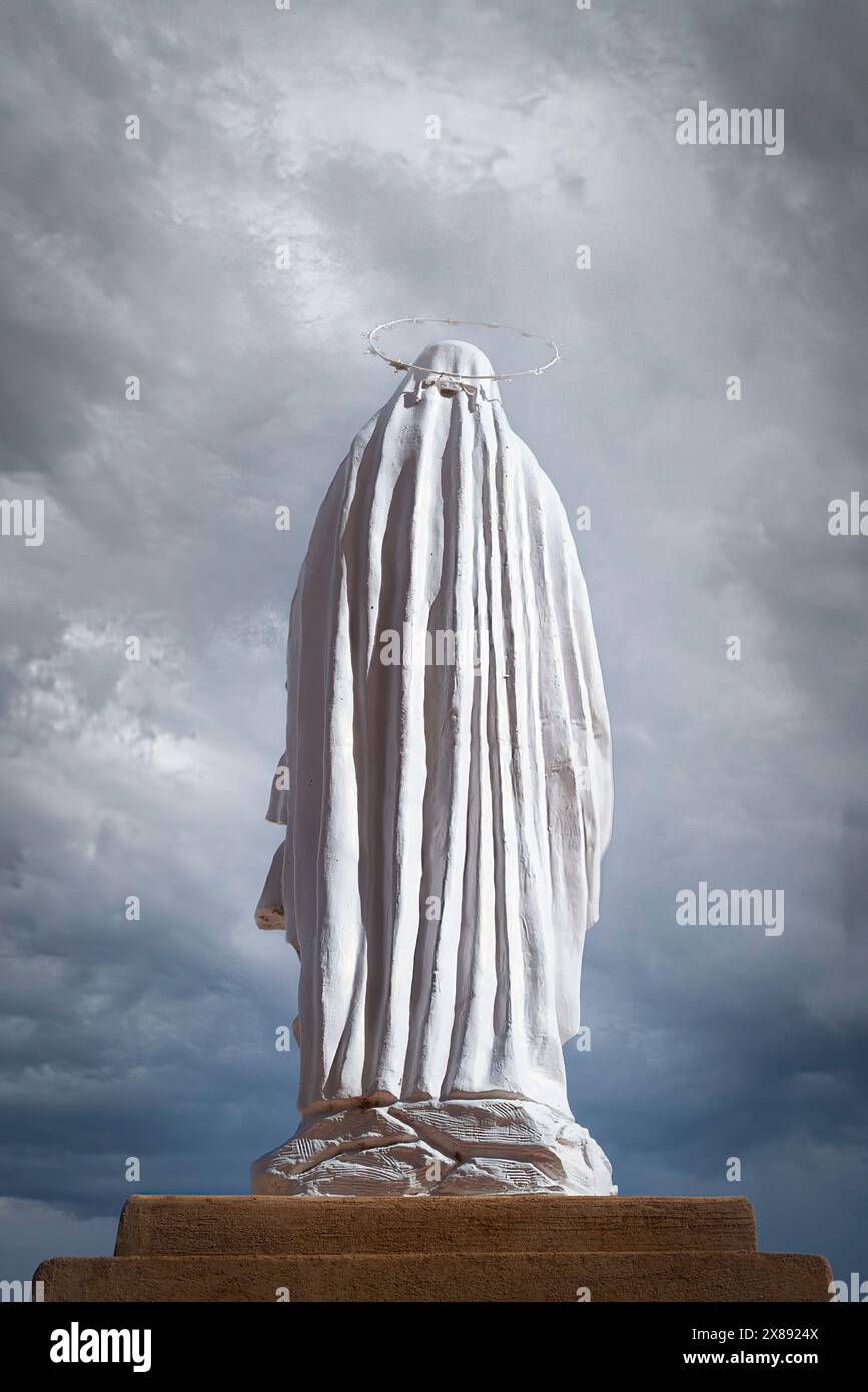 Rear view of the Virgin Mary with halo statue against a stormy sky ...
