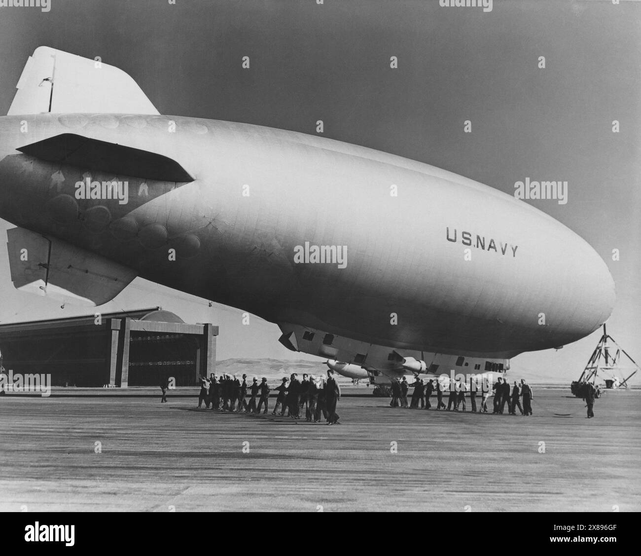 U.S. Navy blimp being held down by a ground crew in front of the hanger ...