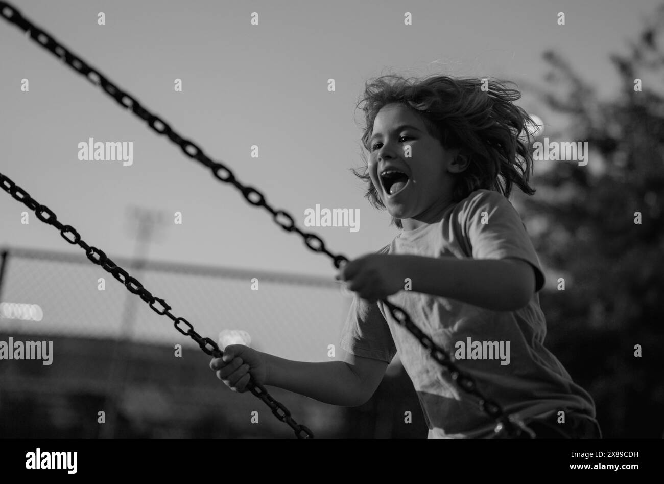 Excited child swinging on chain swing on city kids playground. Swing ride. Cute child having fun ...