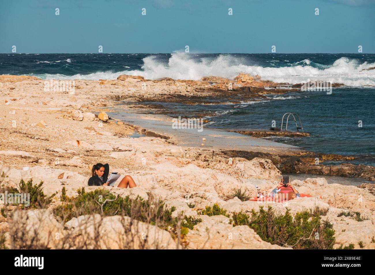 Sunbathers relaxing and reading in the sun on the rocky shores of Qawra ...