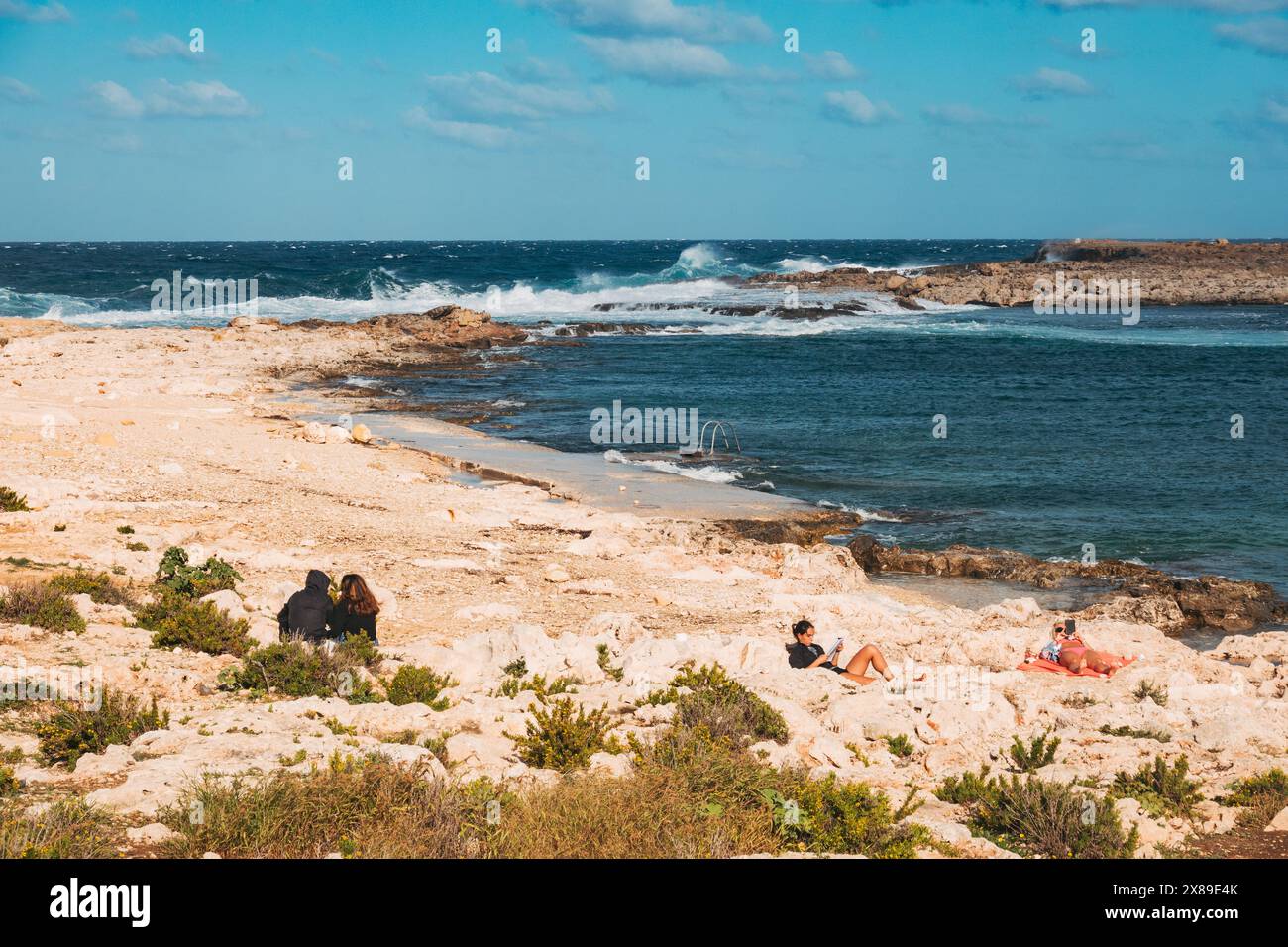 Sunbathers relaxing and reading in the sun on the rocky shores of Qawra ...