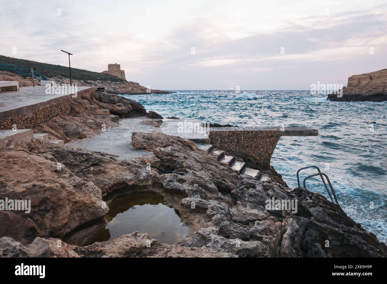Waves crash against rocky terrain as a stone platform leads down to the ...