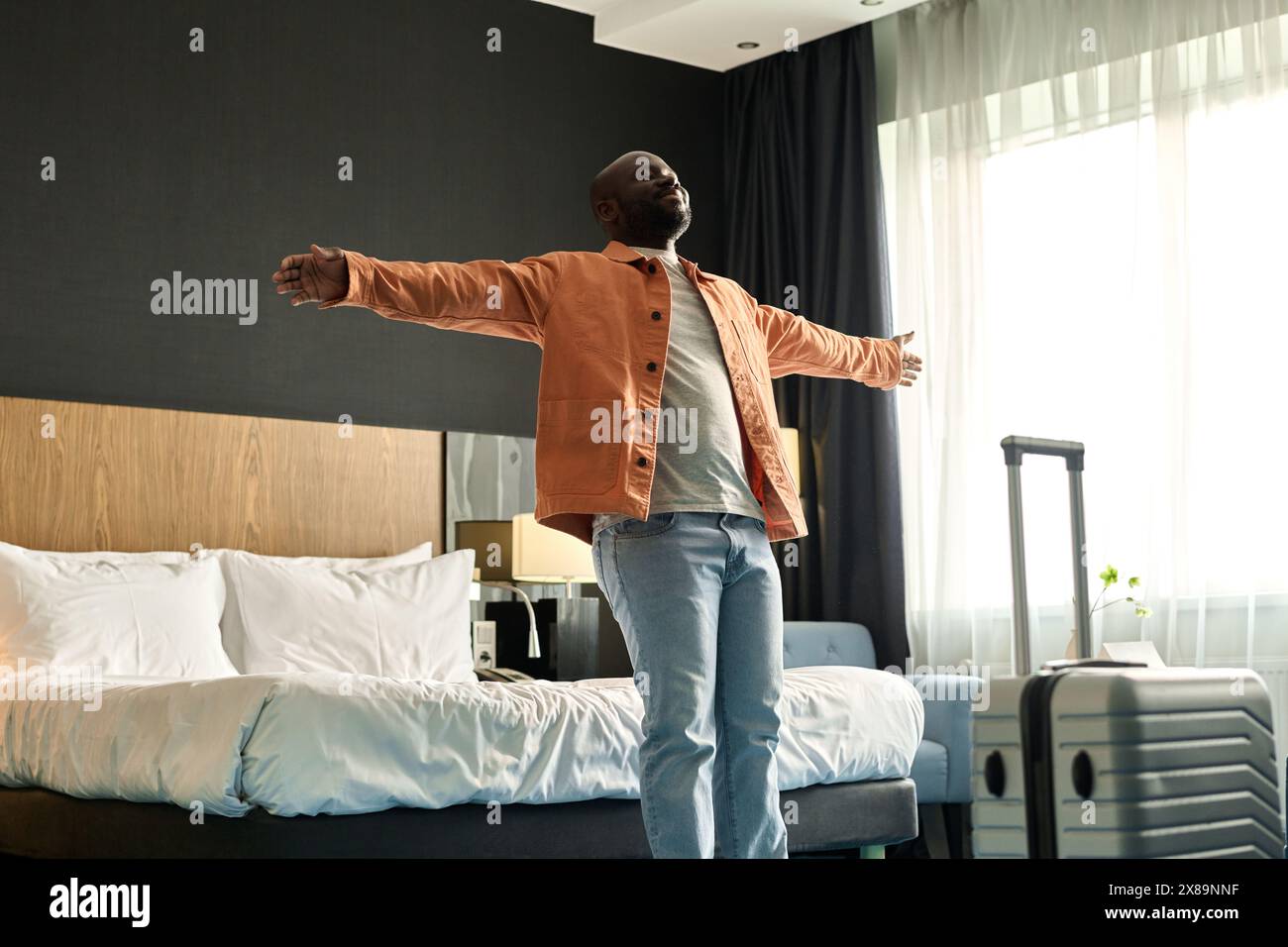 Portrait of joyful Black man falling onto bed with arms spread arriving ...