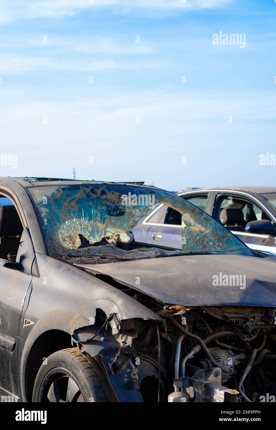 A damaged car is parked in a quiet parking lot, with signs of neglect and wear evident on its ...