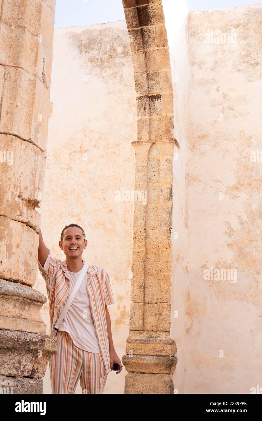 A cheerful young man dressed in a light, striped outfit stands under ...