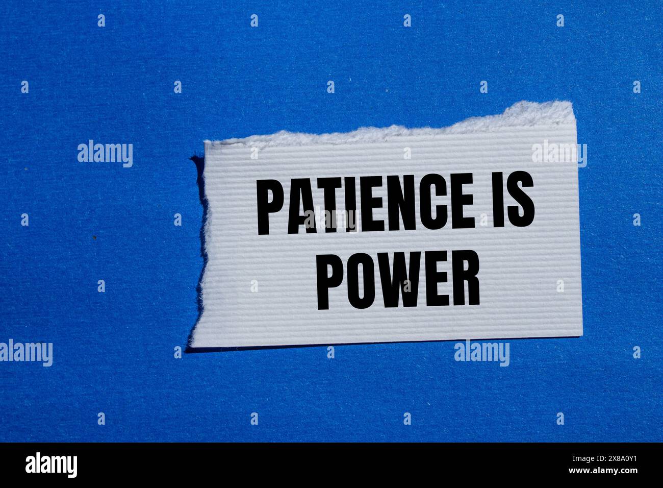 Patience is power words written on ripped white paper piece with blue ...
