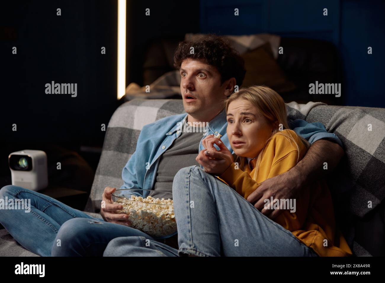 Scared couple watching TV in living room Stock Photo - Alamy