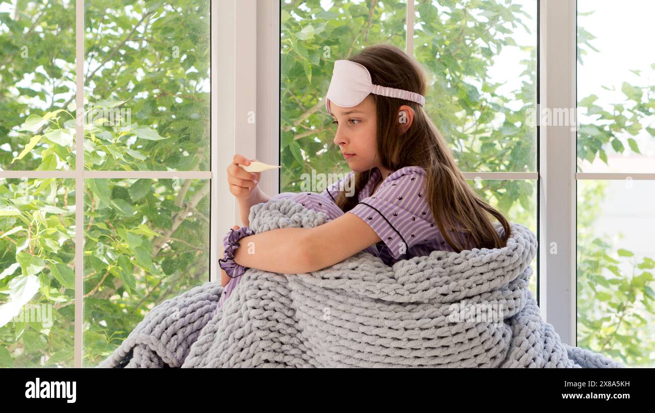 Pensive teenage girl holding an electronic thermometer, showing signs ...