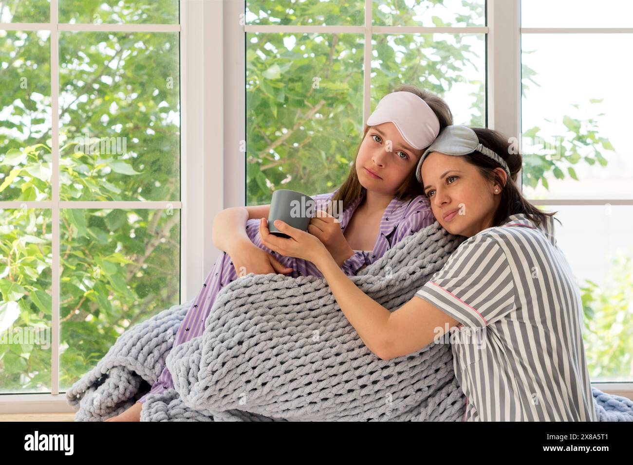 Mother comforting her daughter at home by a sunny window. Common cold ...