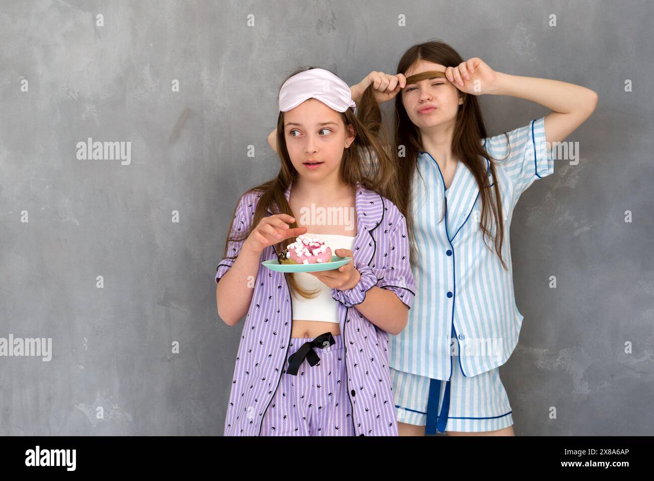 Two girls in pajamas, one eating cake, at a sleepover. Playful and ...