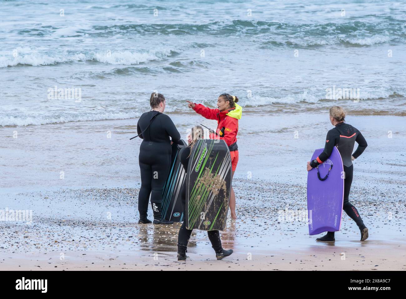 Female bodyboarders talking to a female RNLI Lifeguard on Fistral beach ...