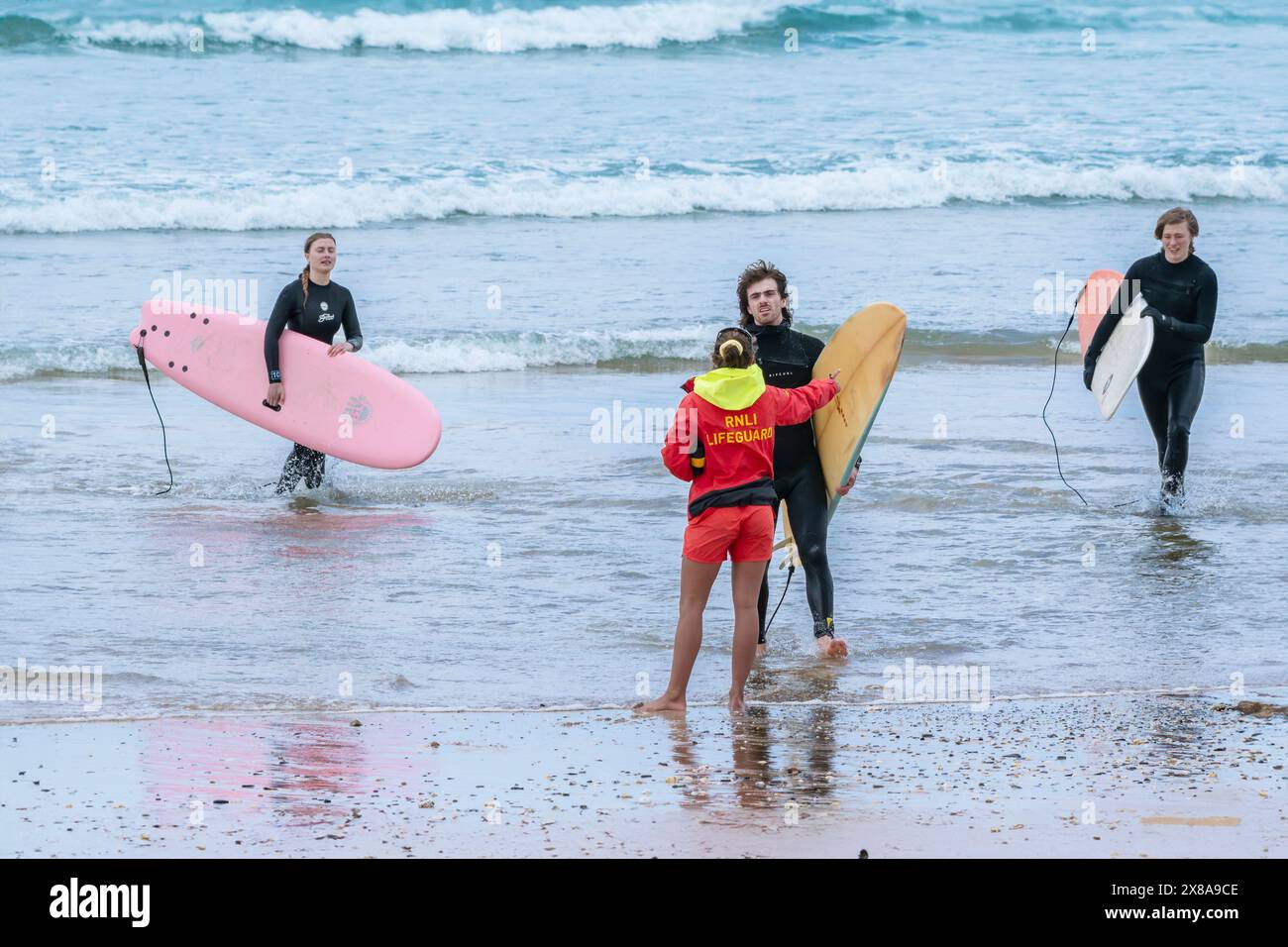 A female RNLI Lifeguard giving safety advice to surfers on Fistral ...
